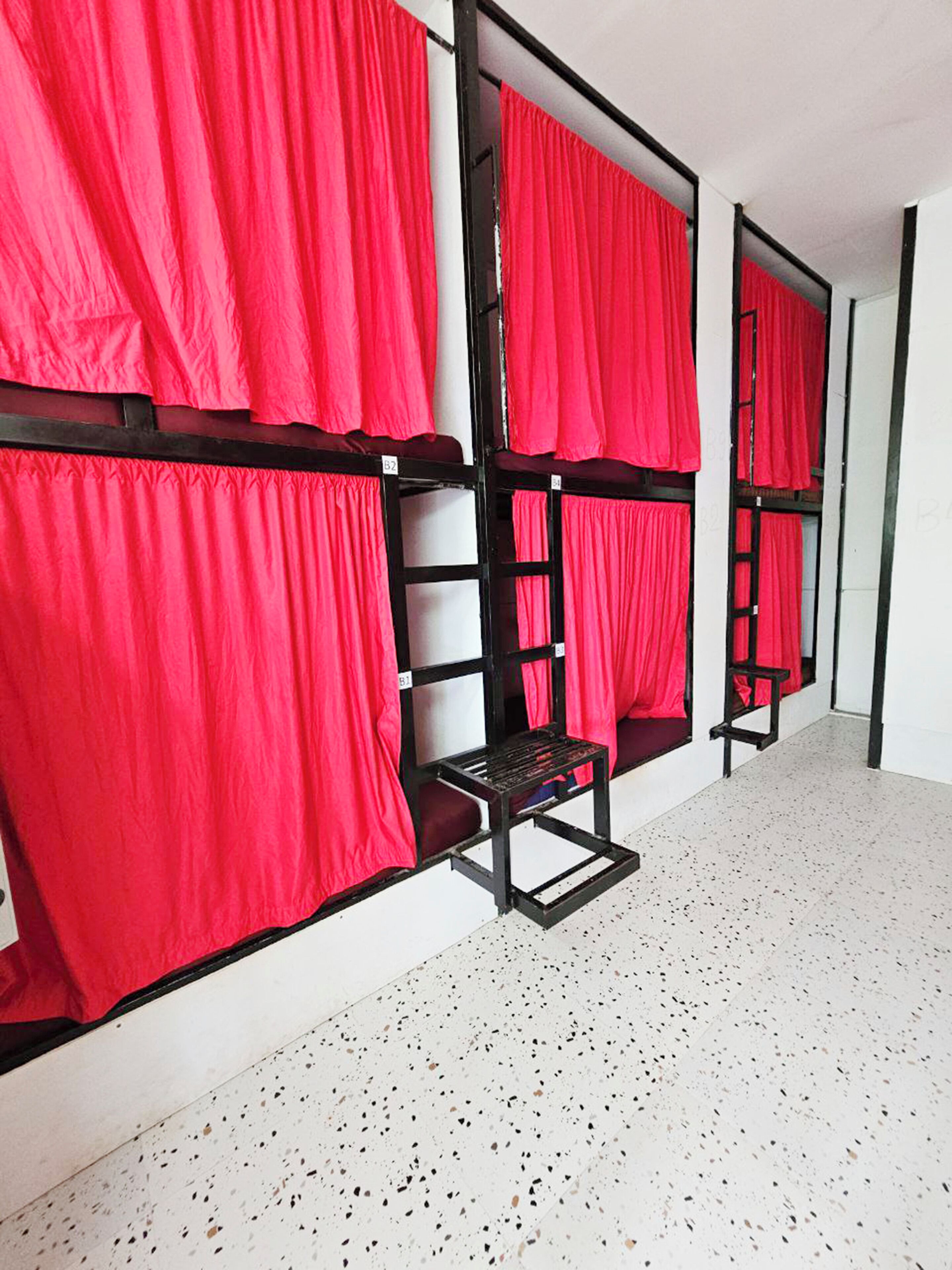 Quarto com beliches, cada um com cortina vermelha. Há um banco no centro.