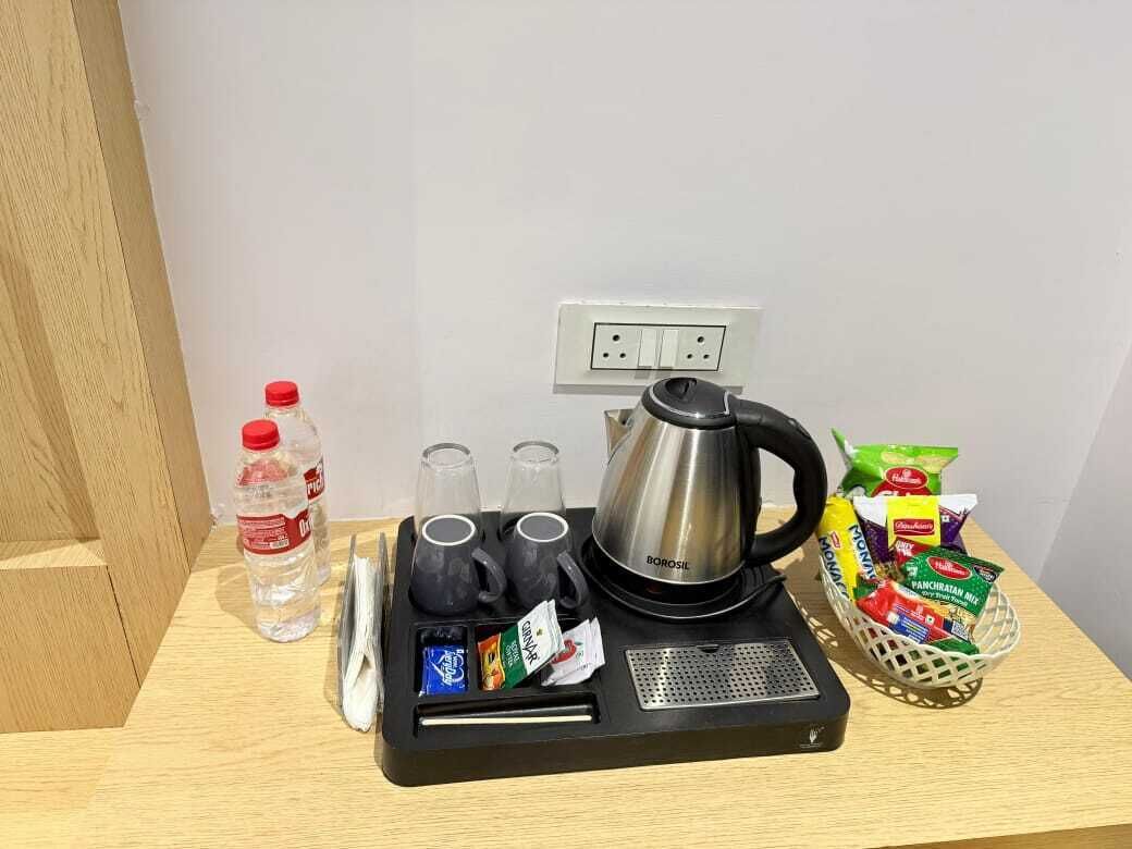 Uma estação de café com cafeteira, xícaras, sachês de açúcar e uma cesta de petiscos.