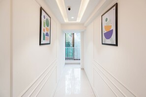 Um corredor com duas obras de arte abstrata emolduradas nas paredes, uma varanda com guarda-corpo e um teto com iluminação embutida.