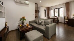Uma sala de estar moderna com um sofá cinzento, uma mesa de centro de madeira e uma mesinha lateral com uma tigela de frutas e um vaso.