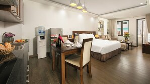 Quarto de hotel com cama, escrivaninha com cadeira, dispensador de água, televisão e área de jantar com mesa e cadeiras.