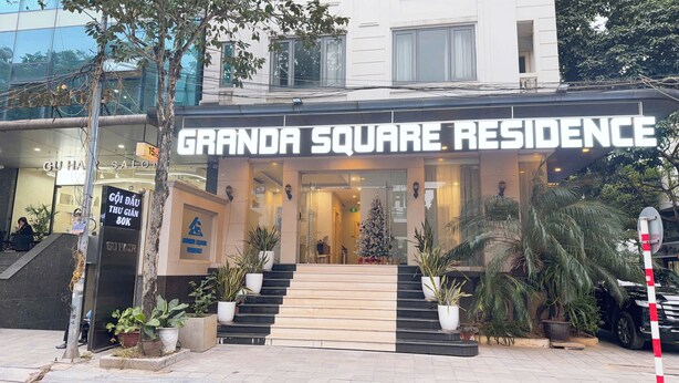 Exterior do Grand Square Residence, com entrada destacada, escadaria que leva à porta, plantas em vasos e um pinheiro de Natal.