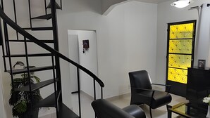 Uma sala de estar moderna com escadaria preta, um sofá de couro preto, uma mesa de centro de vidro e uma janela com moldura amarela.