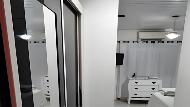 Quarto moderno com porta de vidro para um banheiro, piso de azulejos brancos e cômoda branca com gavetas.