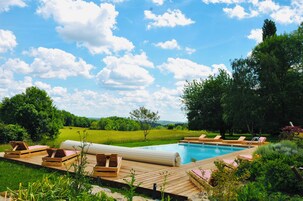 Piscina com deck de madeira e cadeiras de descanso, cercada por vegetação e árvores.