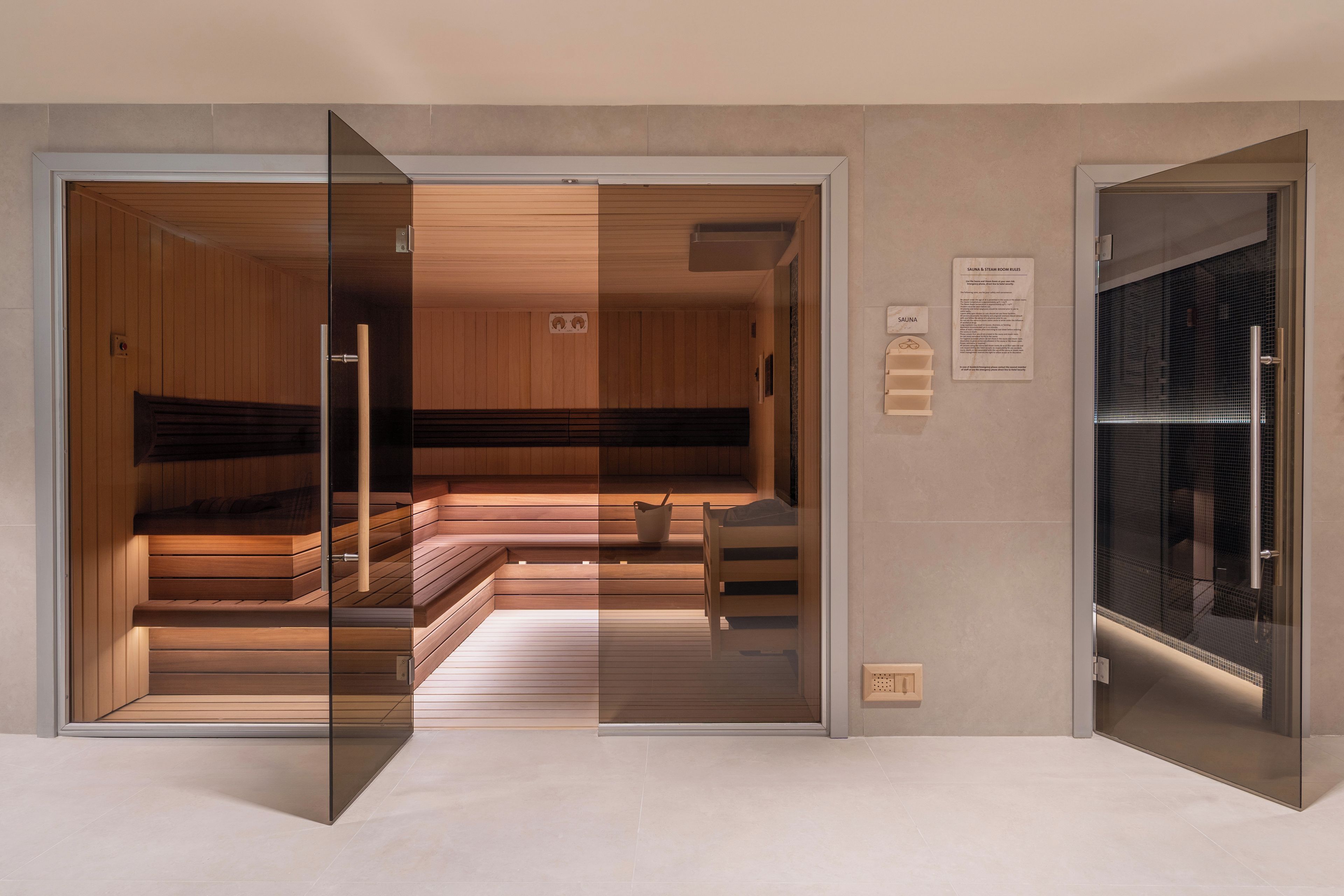 Sala de sauna com bancos de madeira e divisória de vidro.