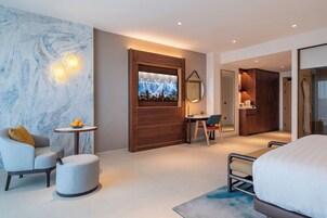 Quarto de hotel moderno com cama, área de estar com mesa pequena, espelho grande e parede com padrão de luz.
