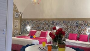Uma sala de estar aconchegante com uma mesa redonda, cadeiras azuis, um sofá com almofadas cor-de-rosa e uma luminária decorativa no teto.