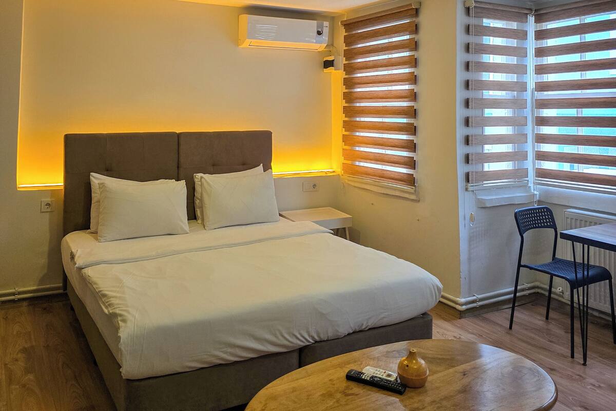 Quarto de hotel com cama, mesa de cabeceira e uma pequena mesa com controle remoto.