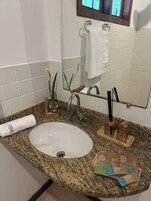 Casa de banho com bancada de granito, lavatório branco, espelho e porta-toalhas.