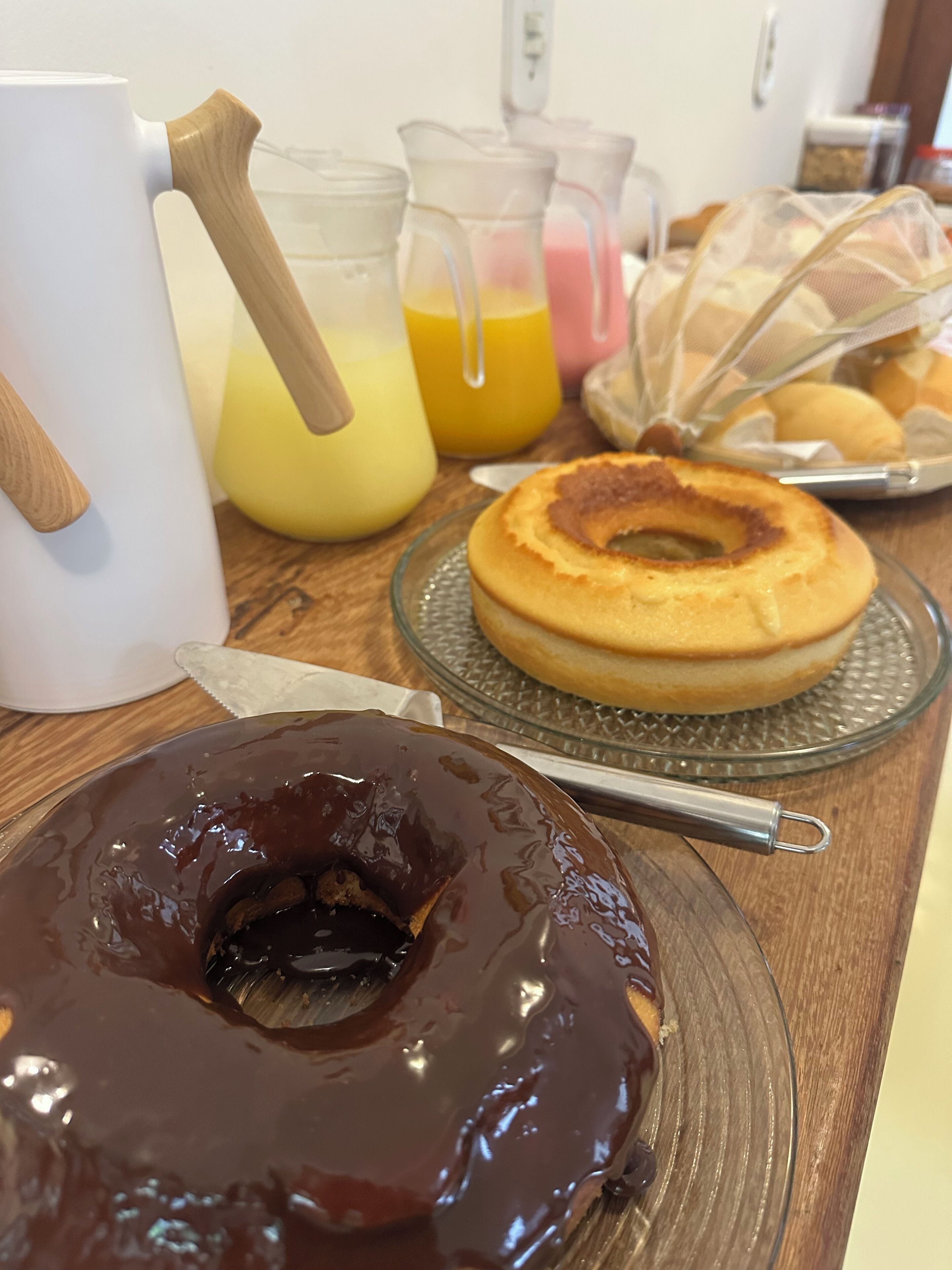 Uma mesa de café da manhã com um donut coberto de chocolate, um jarro de suco de laranja e um prato de doces.