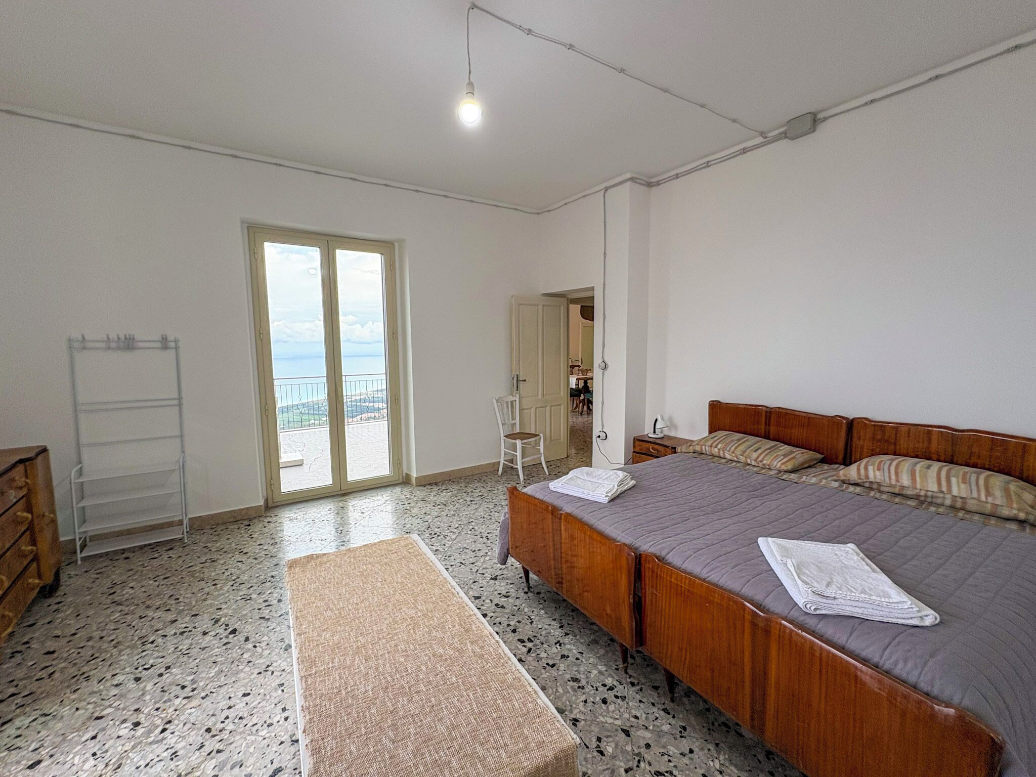 Quarto com cama grande, um banco, guarda-roupa e porta de vidro deslizante para uma varanda.