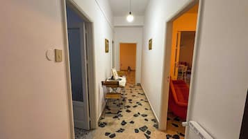 Um corredor estreito com piso estampado, uma porta à esquerda e uma escada à direita.