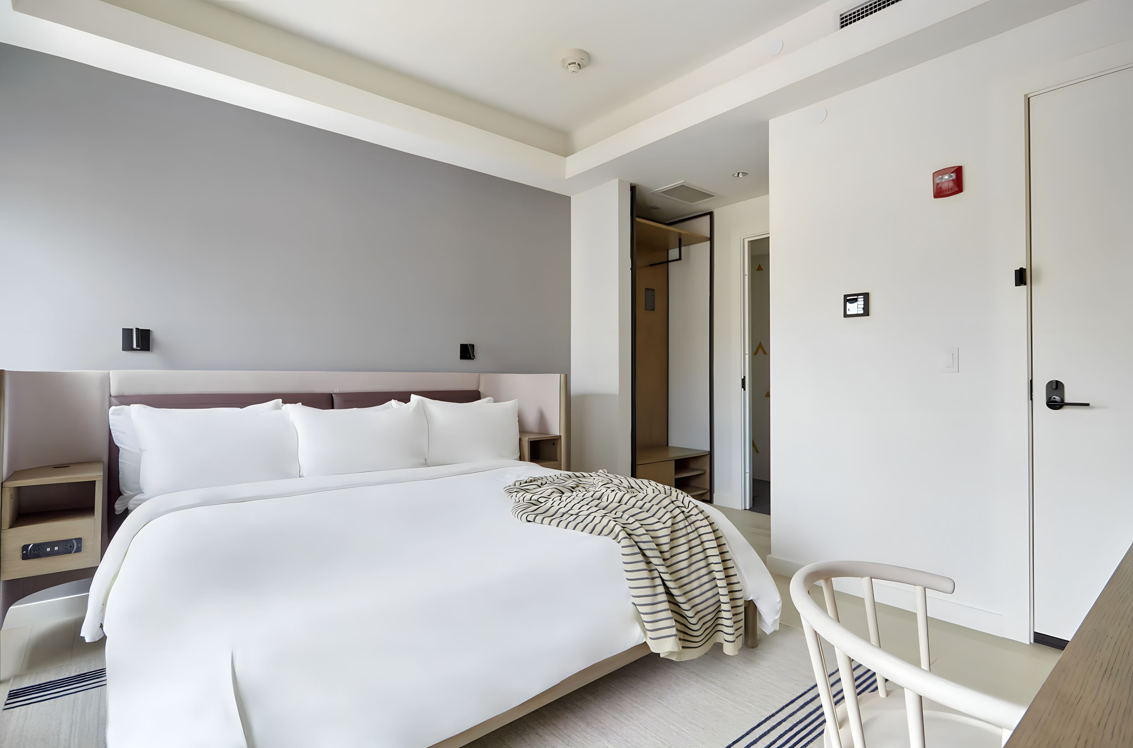 Quarto de hotel moderno com uma cama grande, mesas de cabeceira, guarda-roupa e closet espaçoso.
