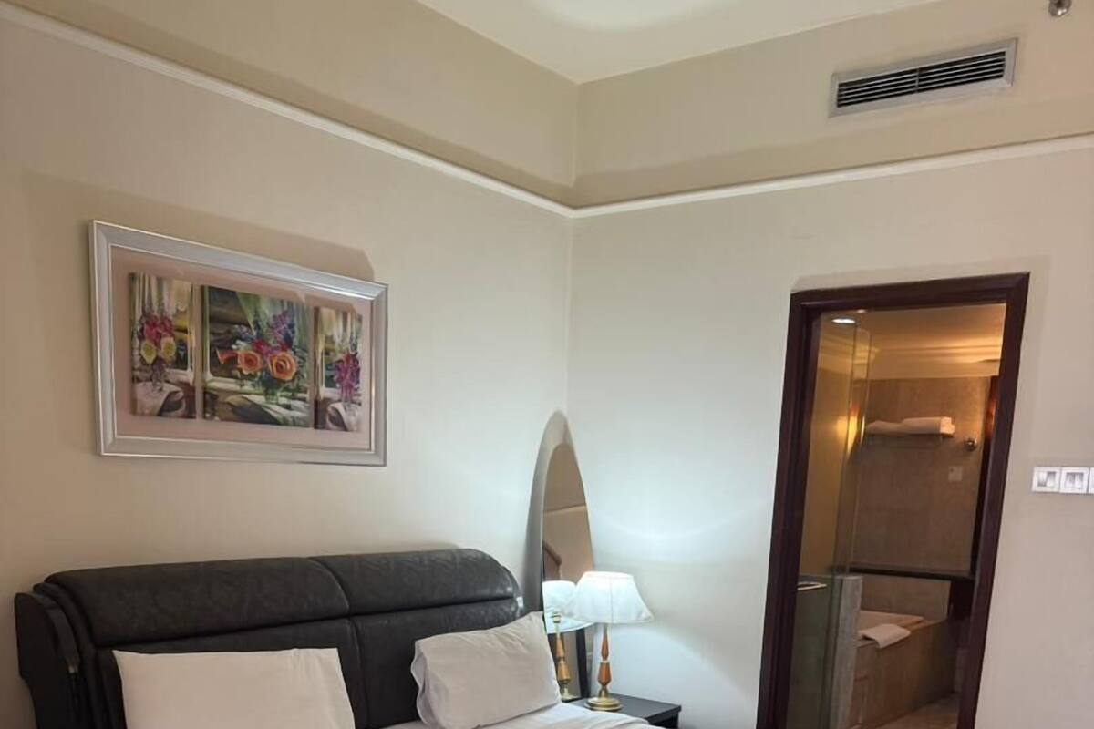 Quarto de hotel com uma cama, mesa de cabeceira, luminária, quadro e porta para o banheiro.