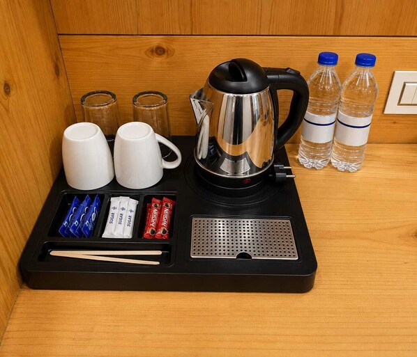 Uma cafeteira, sachês de açúcar, um sachê de açúcar, duas chávenas e duas garrafas de água numa bandeja.