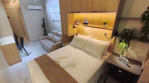 Quarto de hotel moderno com cama, mesa de cabeceira e um pequeno espaço para trabalhar.