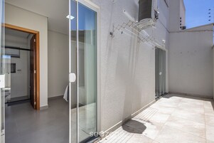 Um espaço residencial moderno com porta de vidro que dá para um banheiro, um pátio ladrilhado e uma parede externa branca.