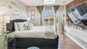 Quarto com cama, um candelabro, uma TV e uma parede com texto decorativo.