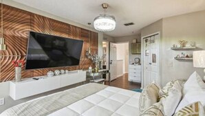 Quarto moderno com uma cama grande, uma TV fixada em uma parede de painéis de madeira e um candelabro.
