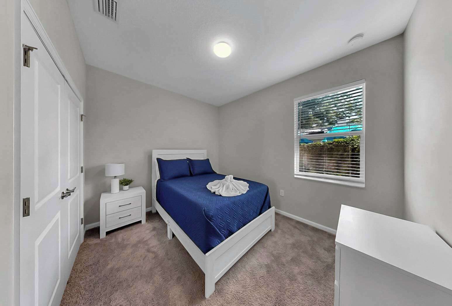 Quarto com cama, mesa de cabeceira, abajur e janela com persianas.