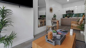 Uma sala de estar moderna com uma mesa de centro de madeira, uma TV fixada na parede e um espaço de jantar com mesa e cadeiras.