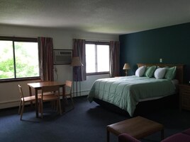 Quarto de hotel com uma cama, escrivaninha, cadeira e janela com cortinas.