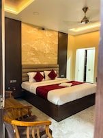 Quarto de hotel moderno com uma cama grande, uma cadeira de madeira, uma escrivaninha e vista para o exterior.