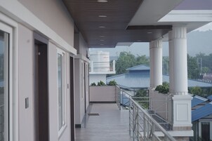 Um corredor com varanda, colunas brancas e vista para edifícios com telhados azuis.