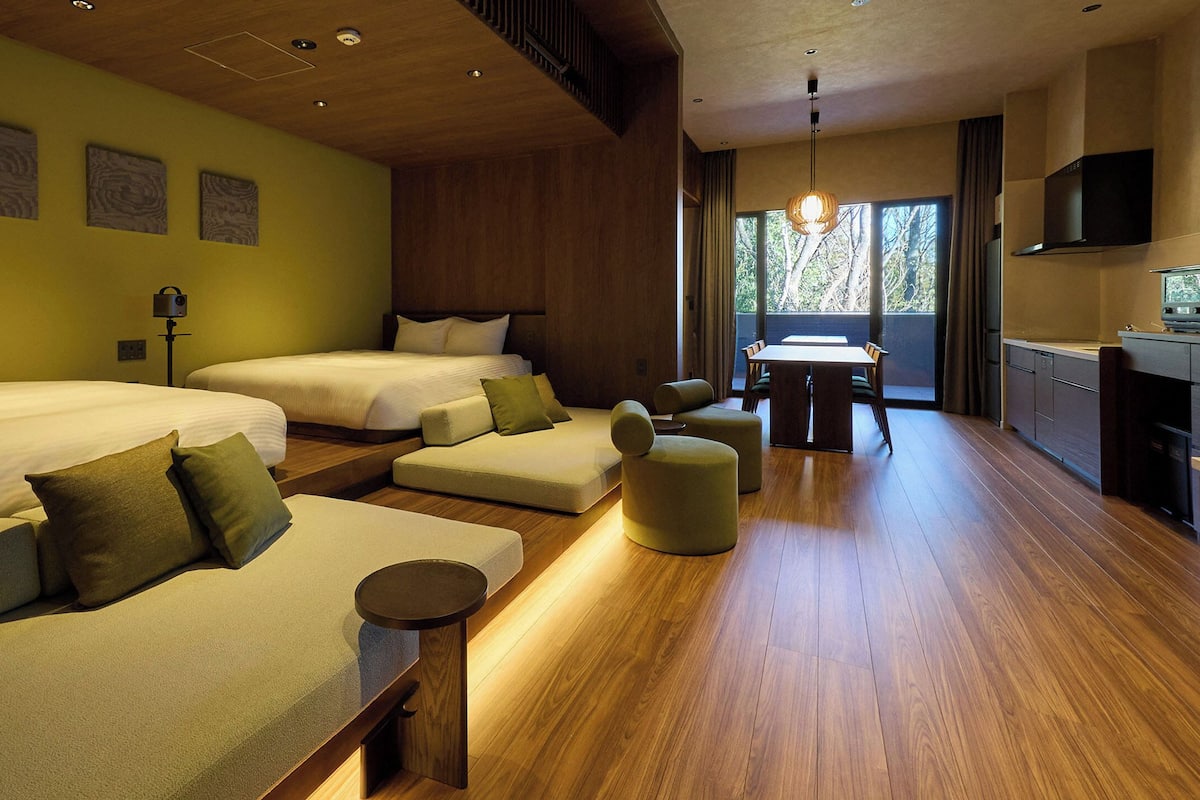 Quarto de hotel moderno com duas camas, área de refeições e cozinha.