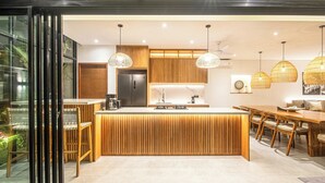 Cozinha moderna com ilha central, armários de madeira, iluminação pendente e área de jantar com uma mesa comprida e cadeiras.