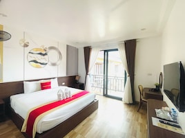 Quarto de hotel com cama, escrivaninha, televisão e varanda com cortinas.