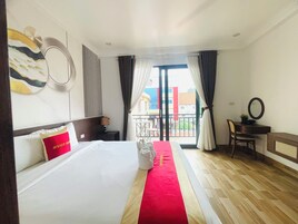 Quarto de hotel com cama, escrivaninha, cadeira, janela com cortinas e vista para prédios.