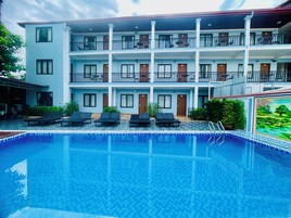Um hotel com vários andares, piscina, espreguiçadeiras e um mural.