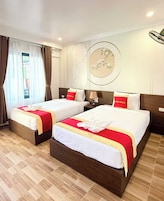 Quarto de hotel com duas camas, cada uma com colcha vermelha e branca, cabeceira de madeira e uma obra de arte circular fixada na parede.