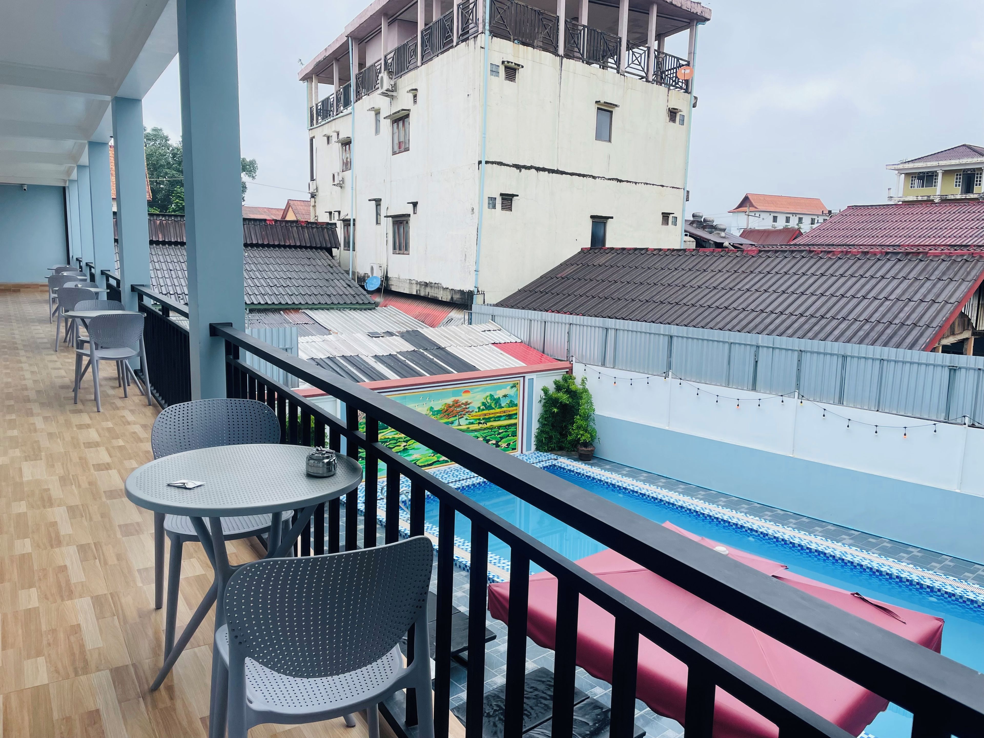 Uma varanda com mesas e cadeiras, uma piscina e vista para edifícios ao redor.