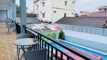 Uma varanda com mesas e cadeiras, uma piscina e vista para edifícios ao redor.