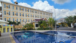 Um hotel com piscina, um edifício grande com várias janelas e um céu azul claro.