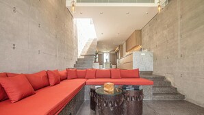 Um interior moderno com um sofá seccional vermelho, uma mesa de centro de vidro e uma escada que leva a um andar superior.
