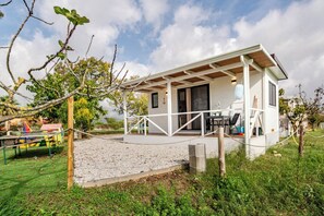 Um pequeno edifício térreo com um alpendre coberto, um jardim cercado e um parquinho ao fundo.