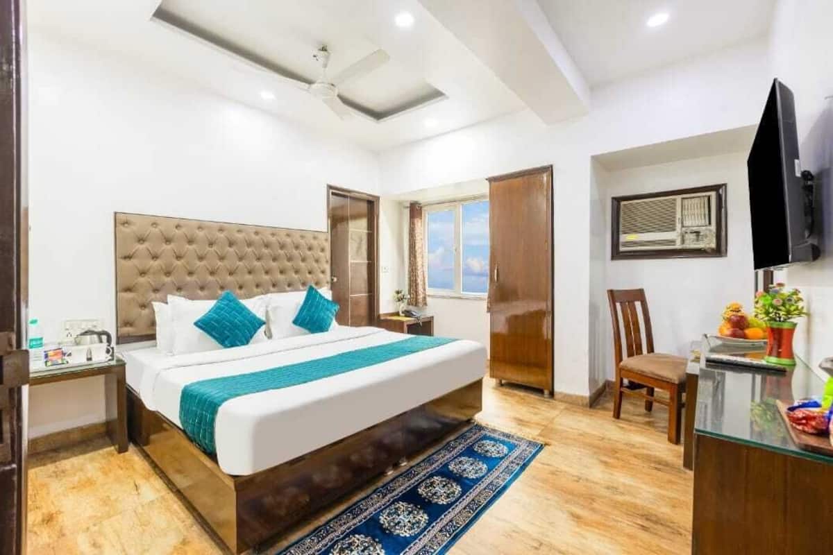 Quarto de hotel com uma cama grande, uma escrivaninha com cadeira, televisão e janela com cortinas.