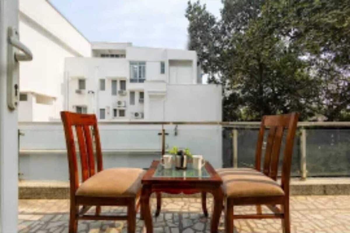 Varanda com mesa e duas cadeiras, vista para um edifício moderno e uma árvore.