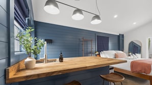 Quarto moderno com cama de madeira, mesa de cabeceira, um criado-mudo e uma janela grande com cortinas.