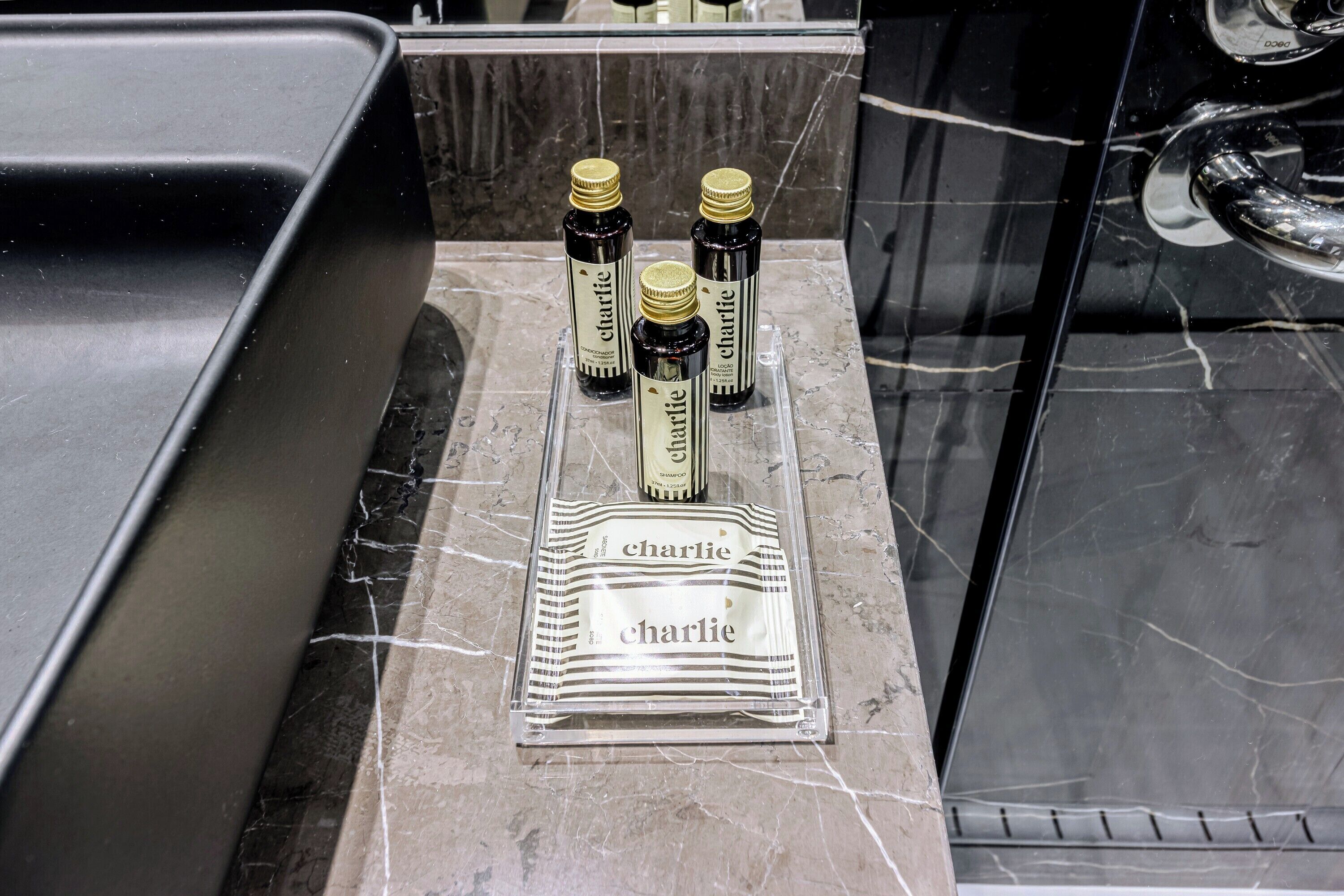 Uma bancada de mármore com três frascos de colônia Charlie e um frasco maior de spray corporal Charlie.