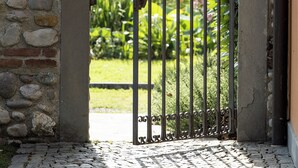 Um arco de pedra com um portão de metal dando acesso a um jardim.