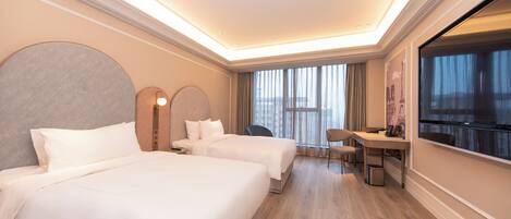 Quarto de hotel com duas camas, uma escrivaninha, uma cadeira e uma janela grande.
