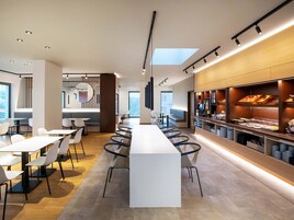 Uma sala de jantar moderna com uma mesa branca comprida, várias cadeiras e um balcão de buffet com diversos alimentos.