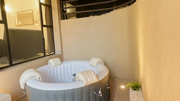 Uma banheira de hidromassagem em área externa coberta, com piso de azulejos e um pequeno jardim.