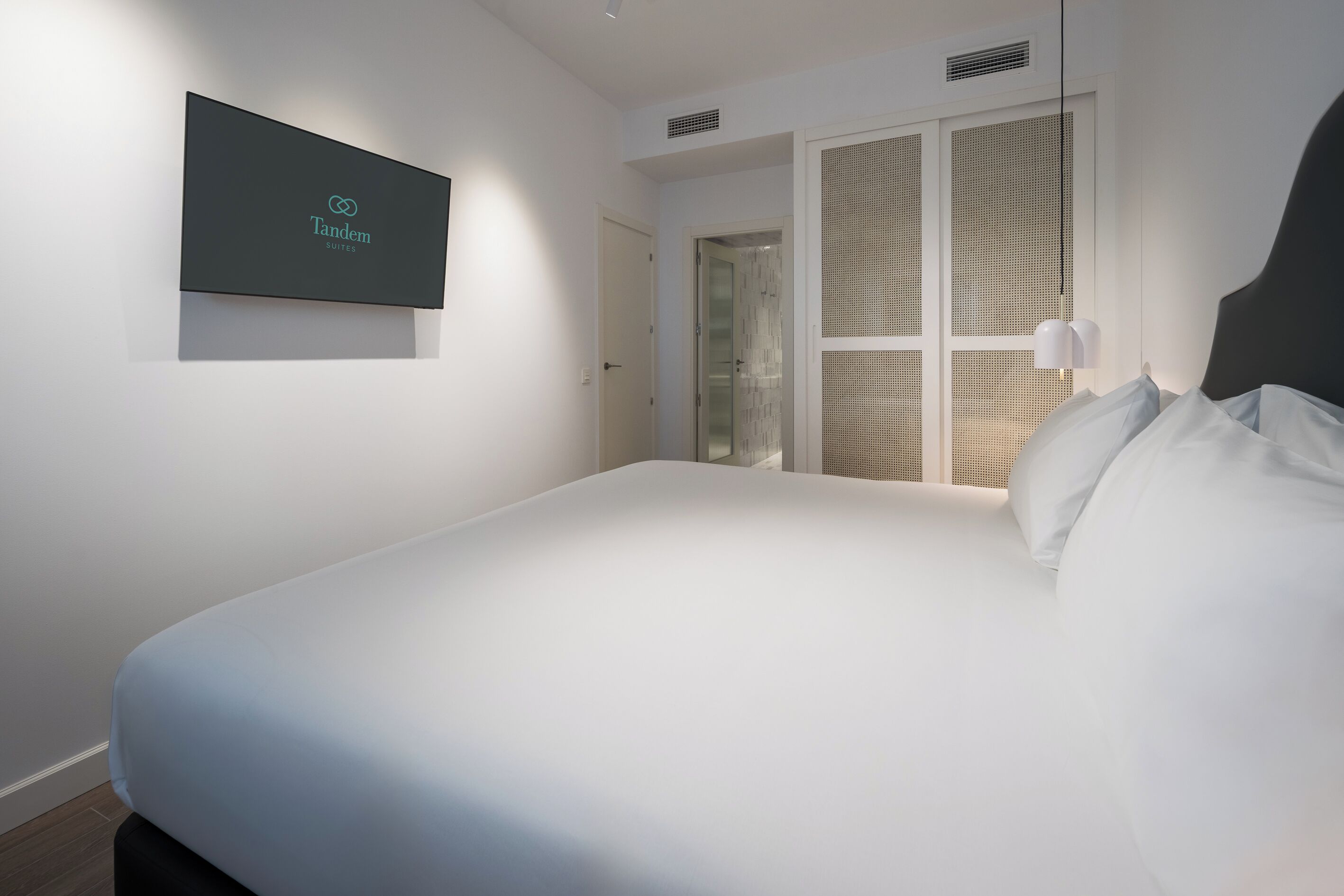 Quarto de hotel moderno com uma cama grande, televisão de tela plana na parede e porta de vidro deslizante para a área do chuveiro.