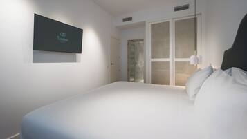 Quarto de hotel moderno com uma cama grande, televisão de tela plana na parede e porta de vidro deslizante para a área do chuveiro.